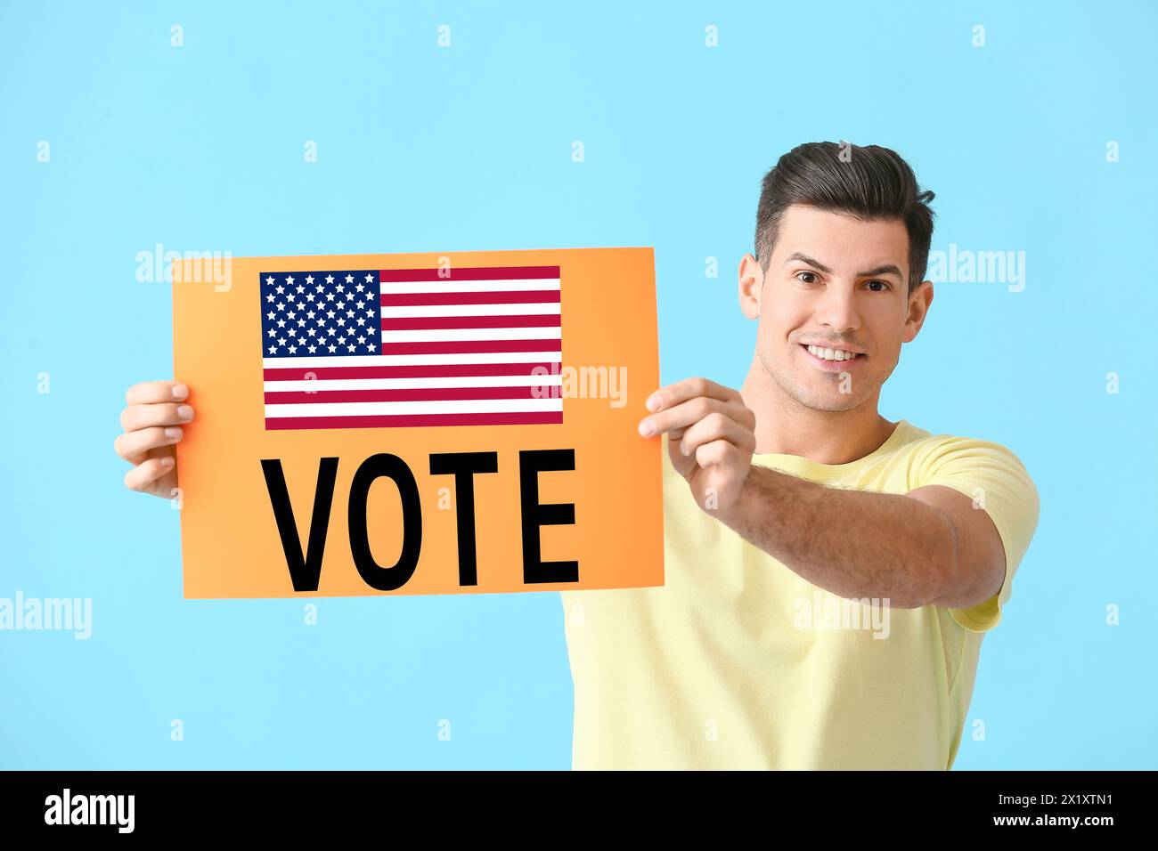 Young man holding poster with word VOTE and USA flag on light blue ...