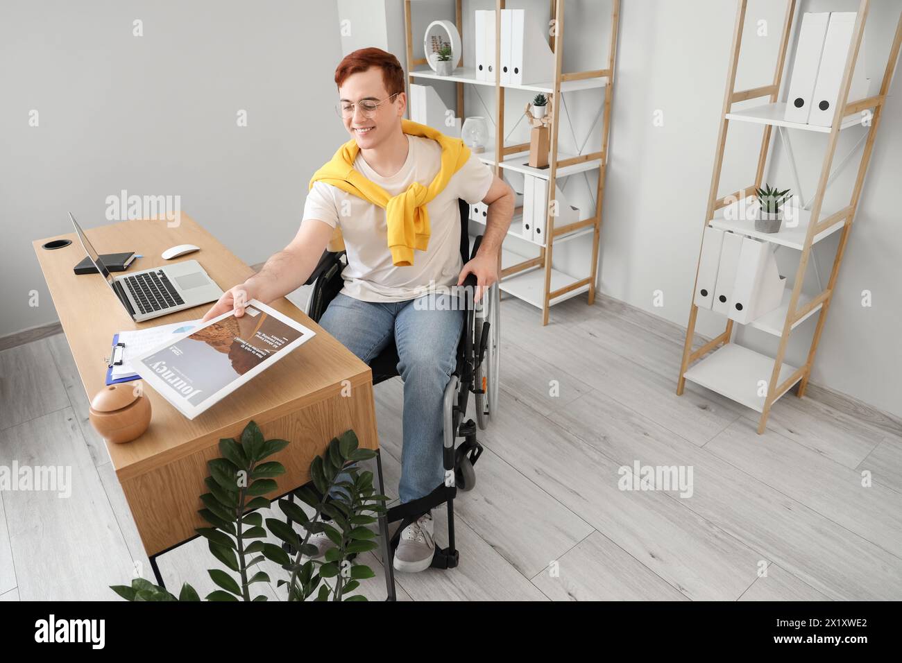Young man in wheelchair with magazine on table at office Stock Photo ...