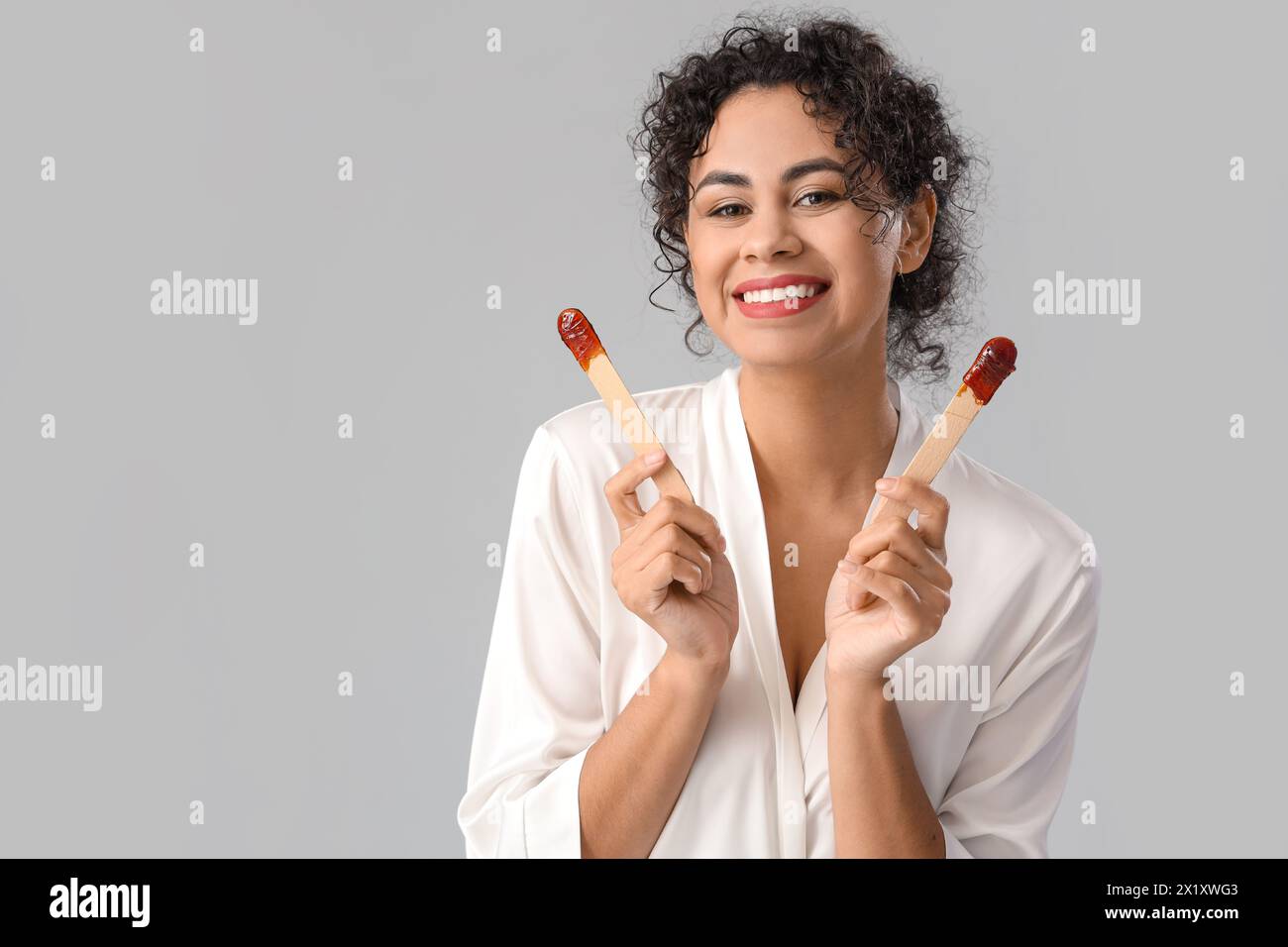 Beautiful African-American woman with sugaring paste on grey background ...
