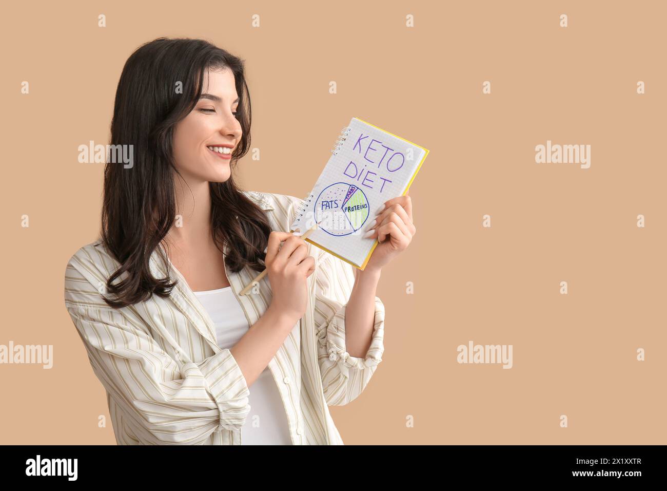 Happy smiling young woman pointing at notebook with keto diet chart on ...