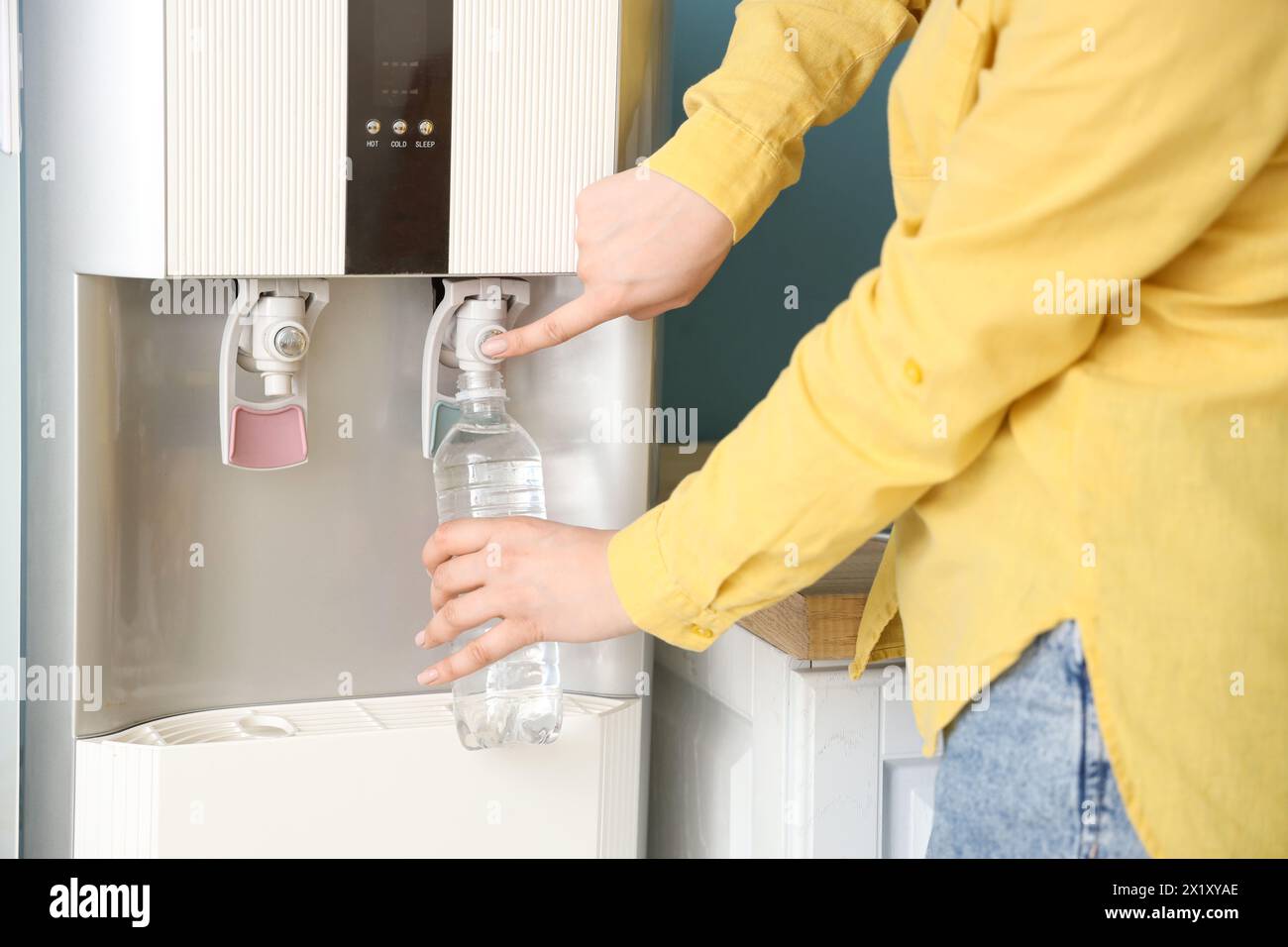 Woman filling plastic bottle with filtered water from cooler near blue ...
