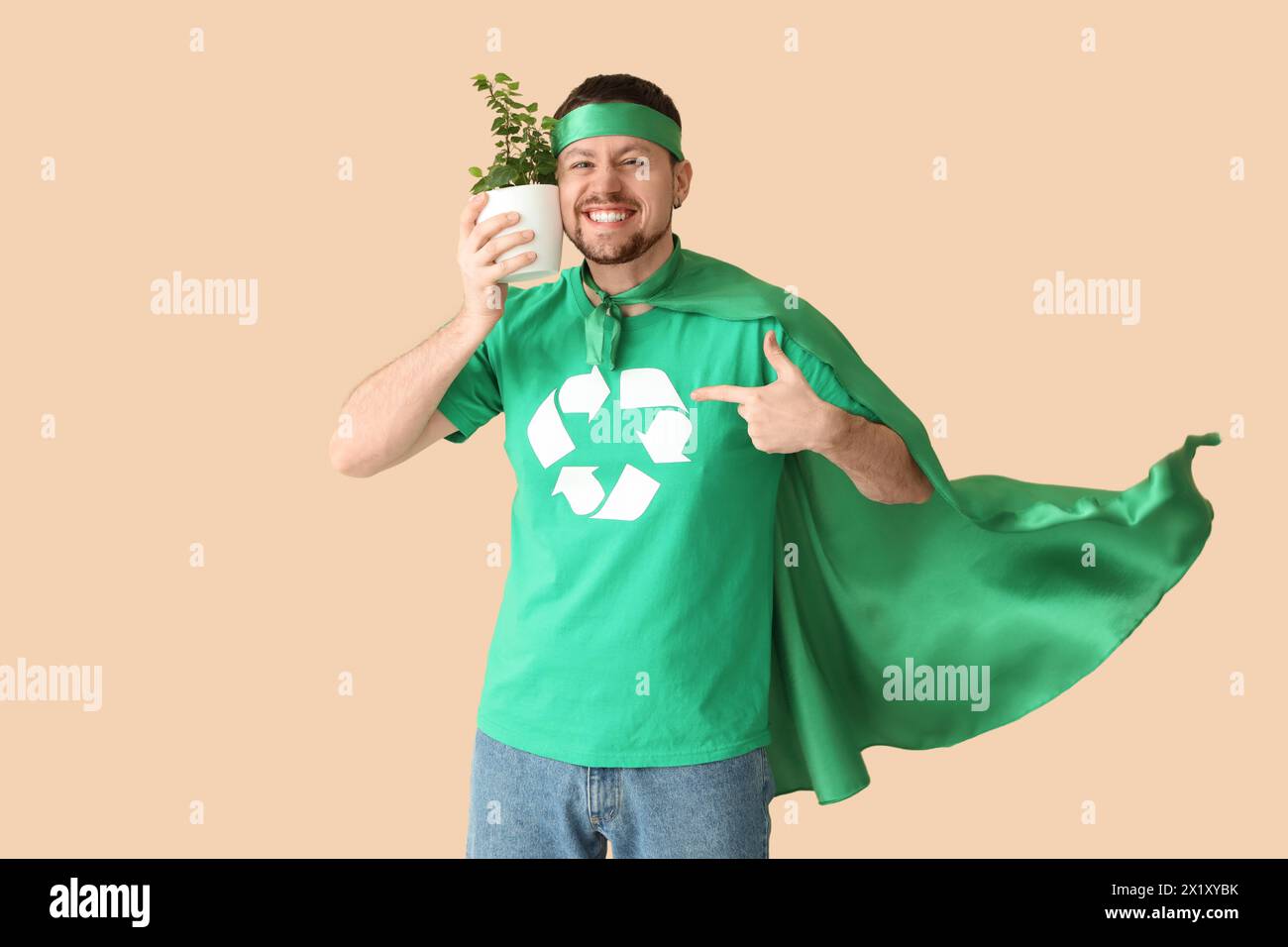 Young man dressed as eco superhero with houseplant pointing at ...