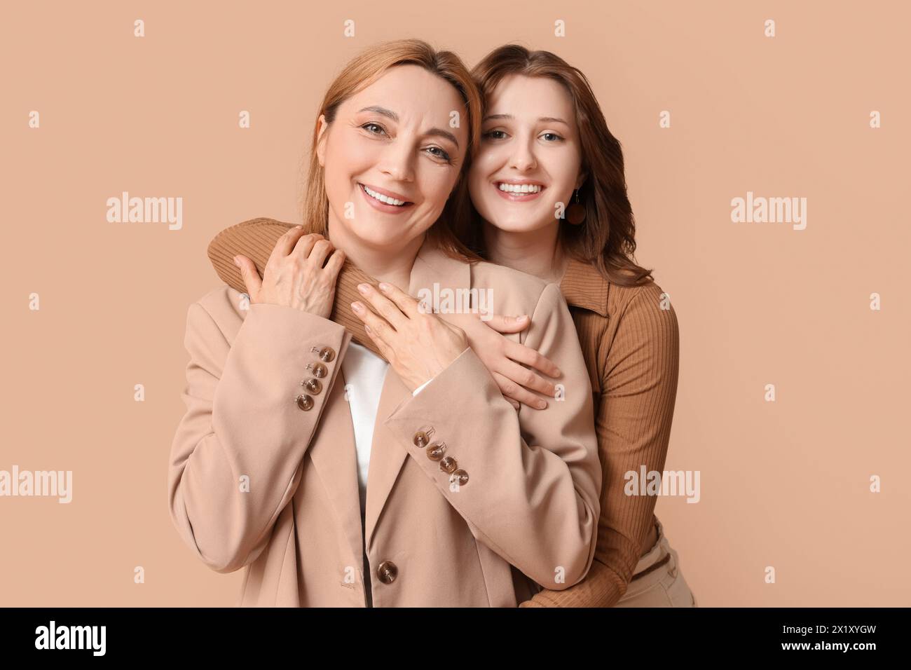 Beautiful mature woman with her daughter hugging on brown background. Mother's Day celebration ...