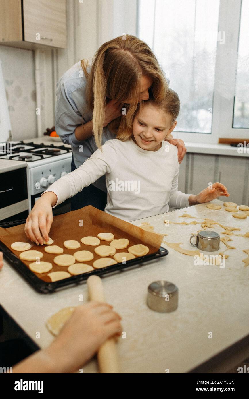 A woman is assisting a young girl in baking cookies in a kitchen setting. The woman is guiding ...