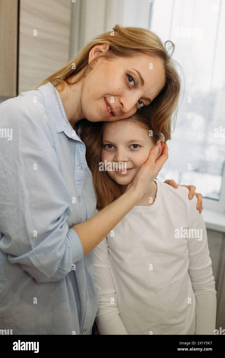 A woman is embracing a young girl in a warm hug in the kitchen. The two ...