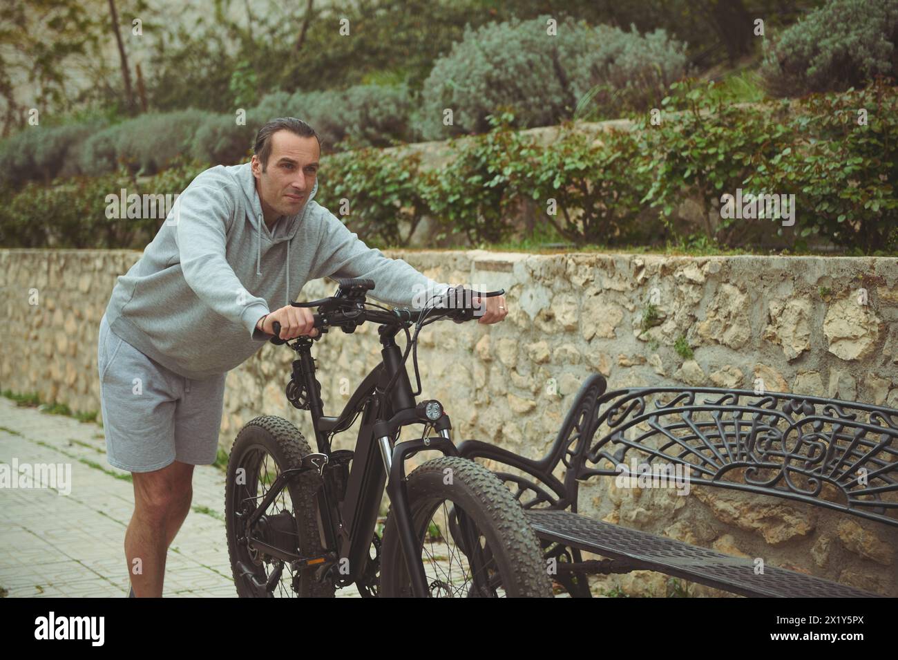 European young man pushing his electric mountain bike up the street ...