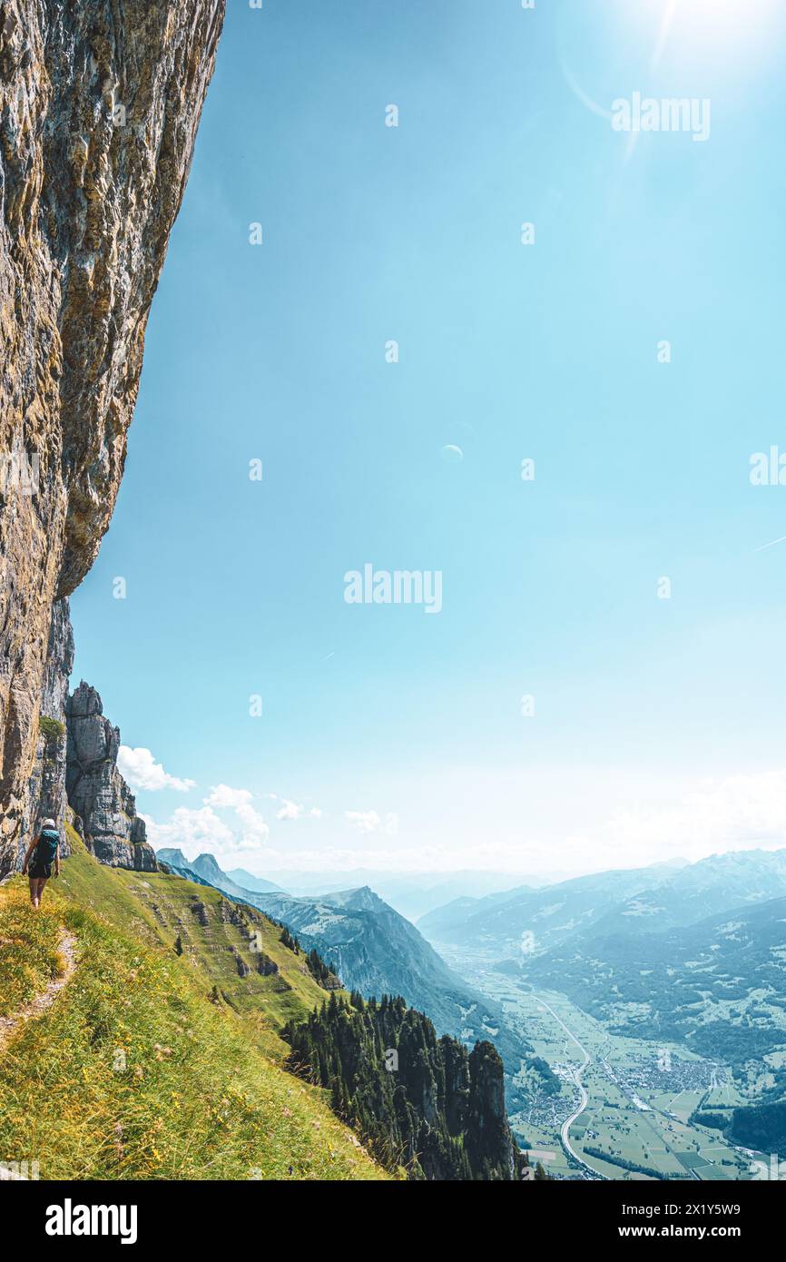 Description: Mountaineer hikes on alpine trail under steep rock wall ...
