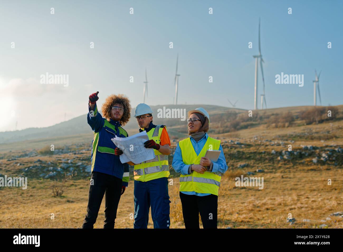 A team of engineers and workers oversees a wind turbine project at a ...
