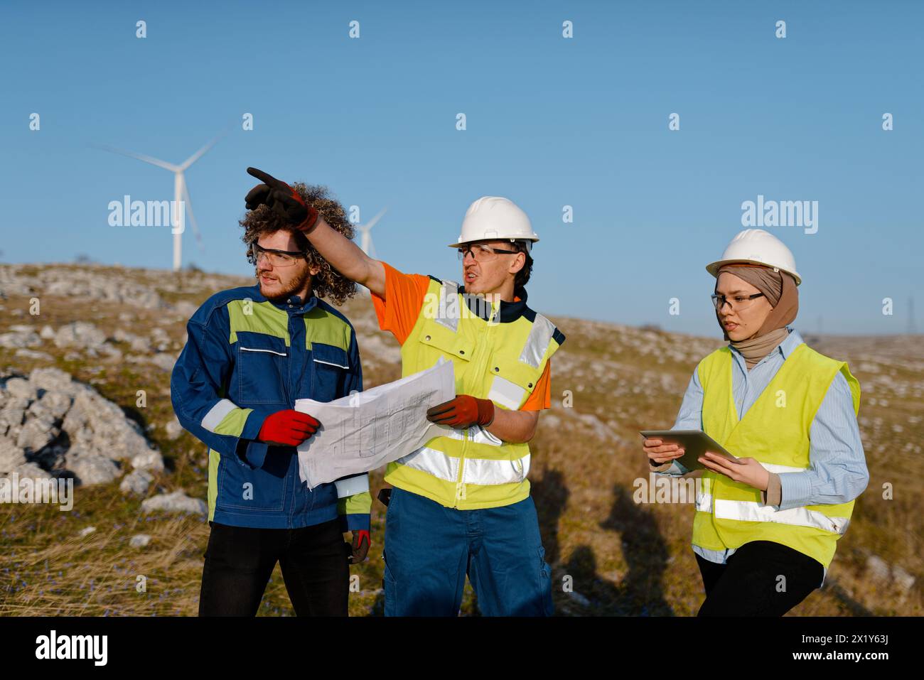 A team of engineers and workers oversees a wind turbine project at a ...