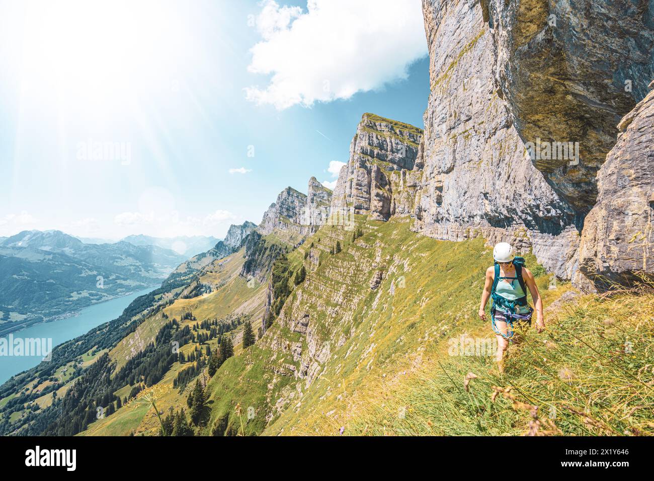 Description: Sporty woman hiking on meadow below steep rock wall with ...