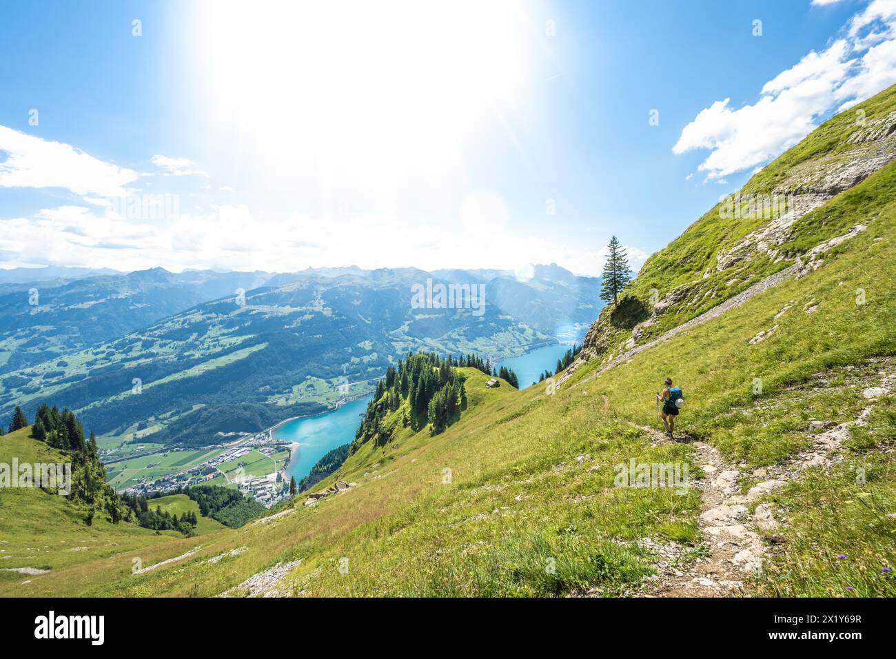 Description: Athletic woman hikes on flowery trail on steep meadow with ...