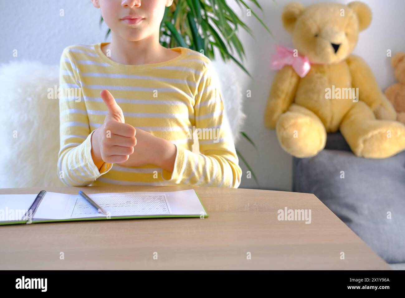 child, schoolboy in yellow t-shirt doing homework at the desk, holding ...