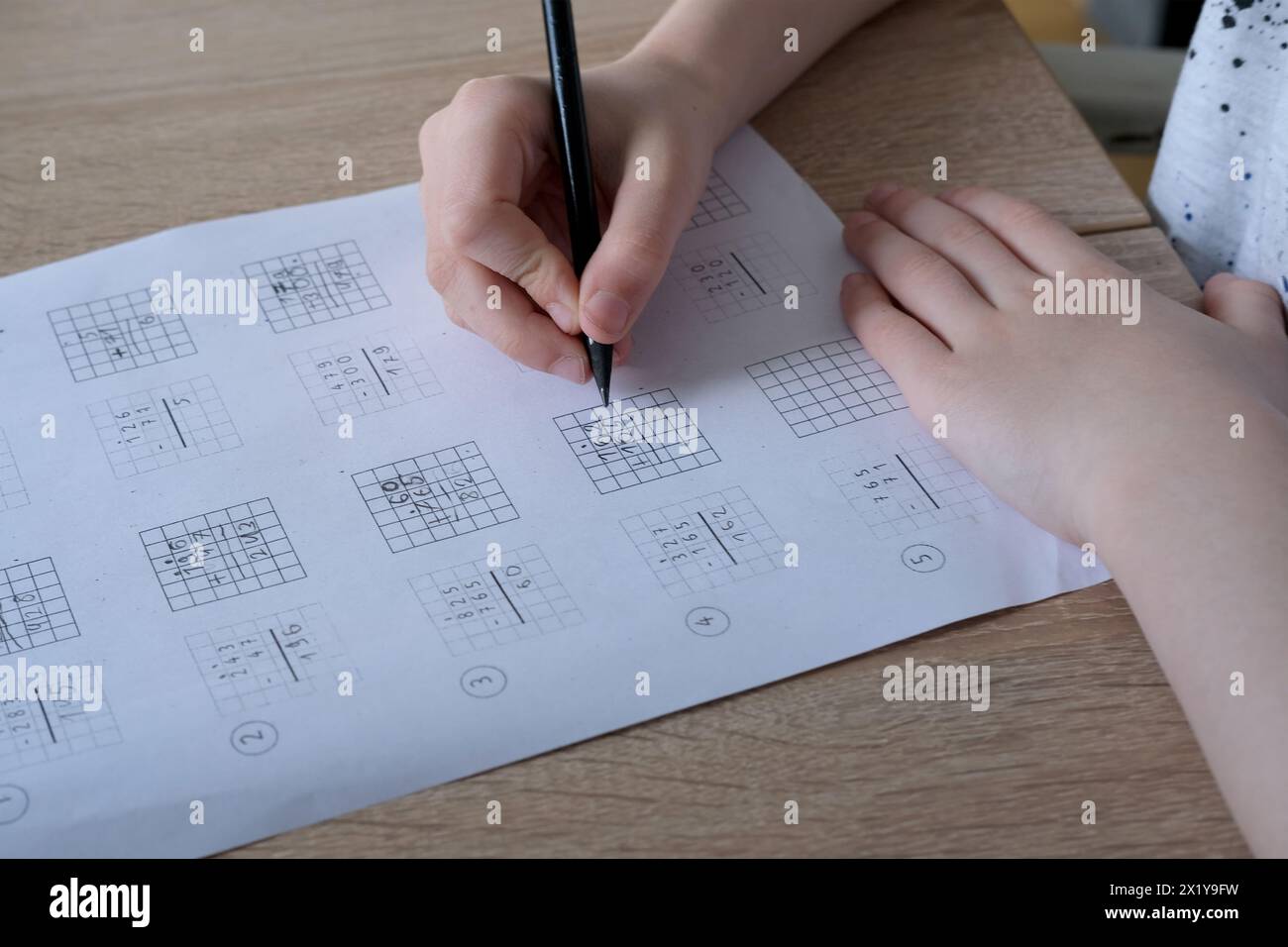 child, schoolboy solves math examples in a column, makes arithmetic ...