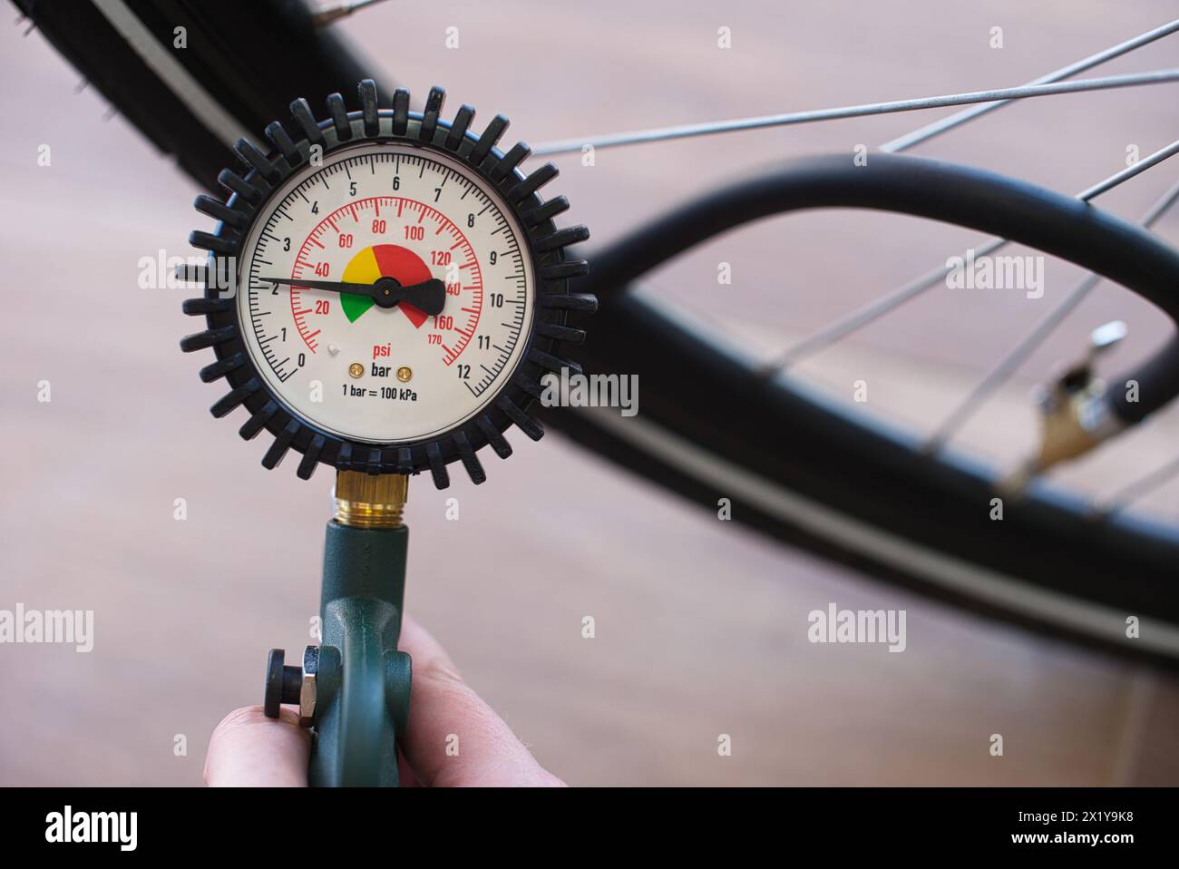 Hand holding a tire pressure gauge indicating 2.2 bar or 31 psi. Blurry ...