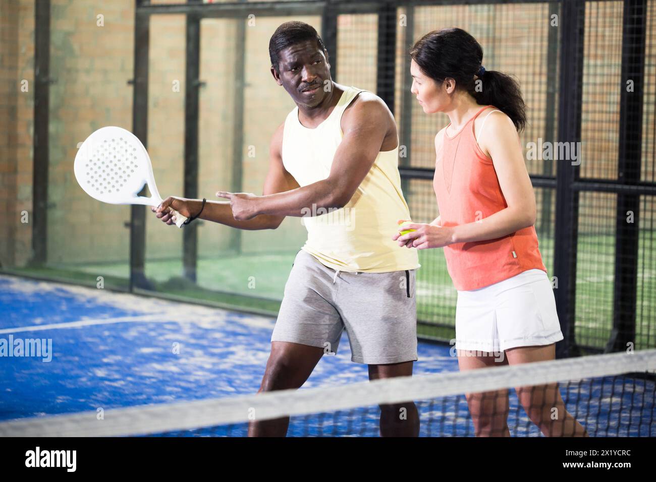 African american trainer teaches woman to play padel on tennis court ...