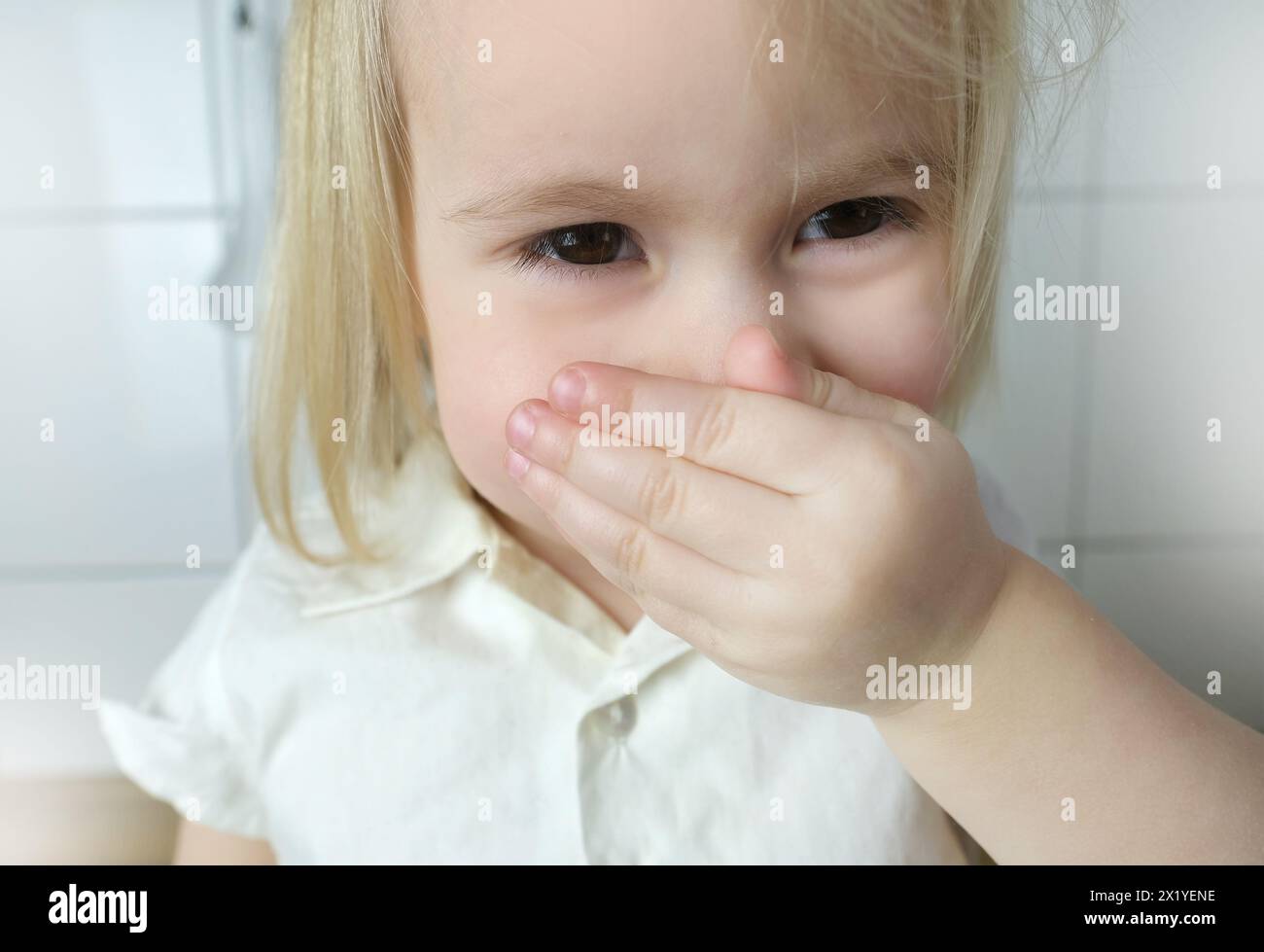 small child, baby, blonde girl covered her mouth with her palm, the ...