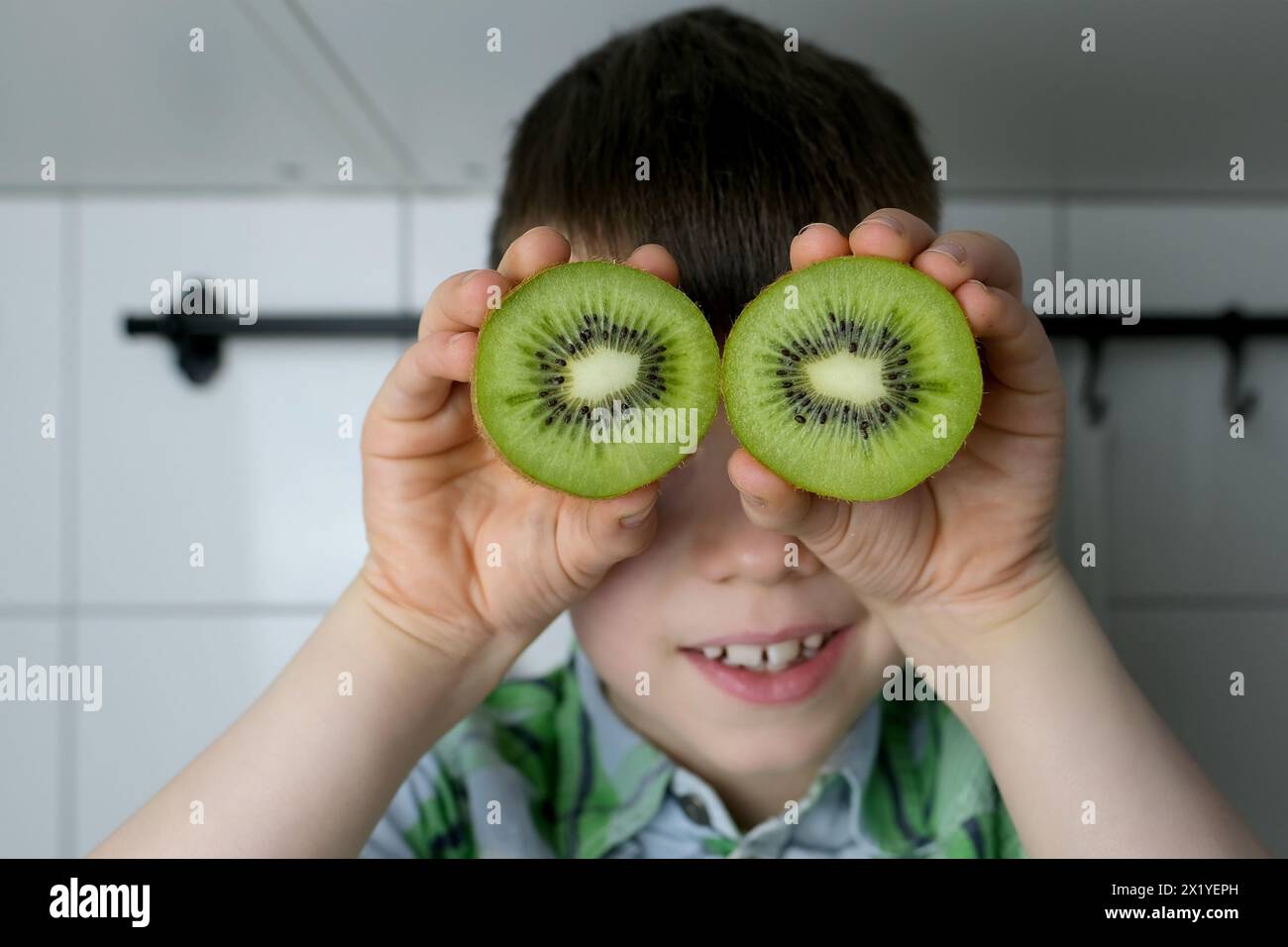 child, kid 8-10, boy sitting in the kitchen at home, juicy cut green kiwi instead of eyes, head ...