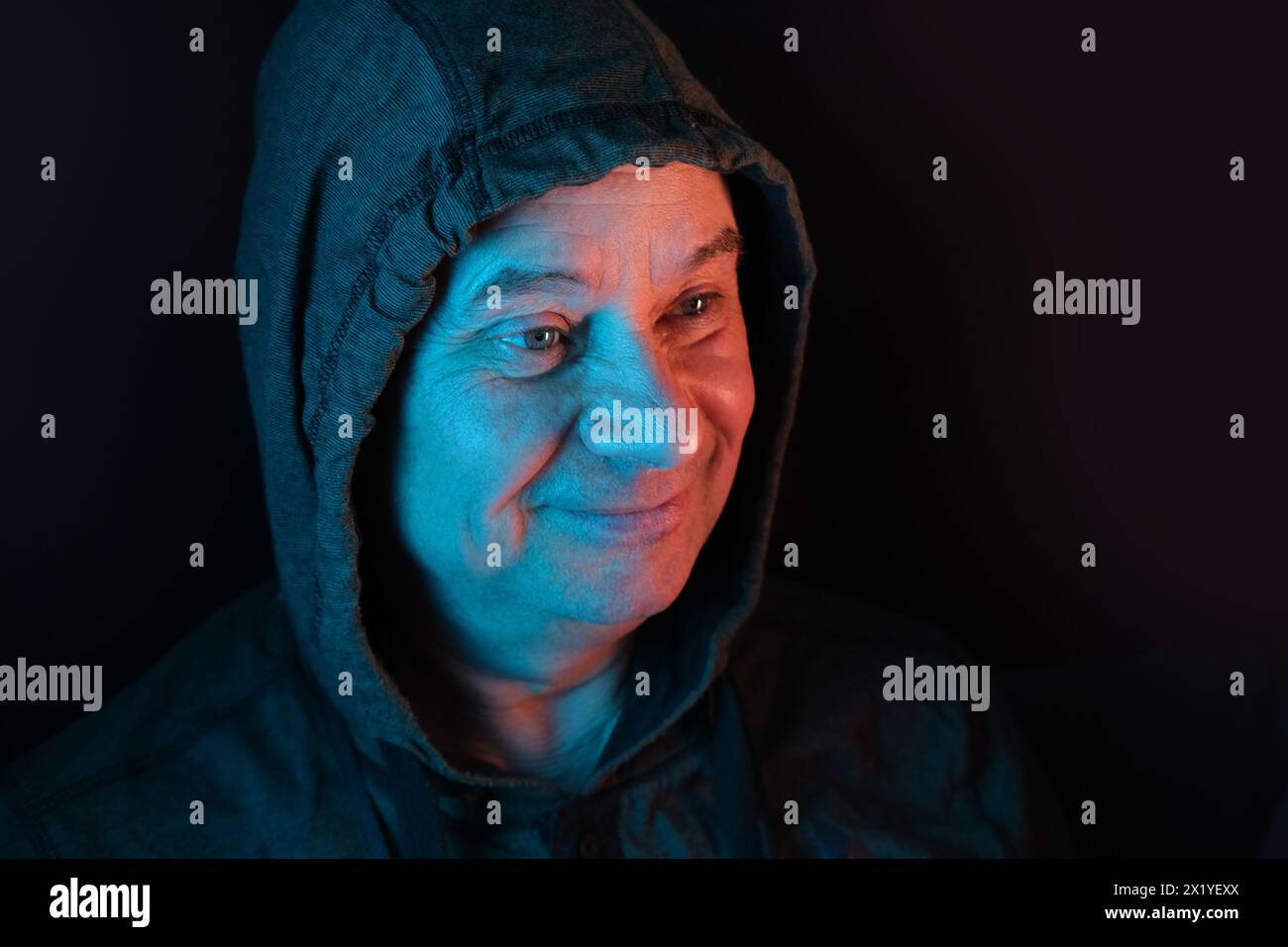 close-up face of an elderly man, a senior in a black hood in a dark ...