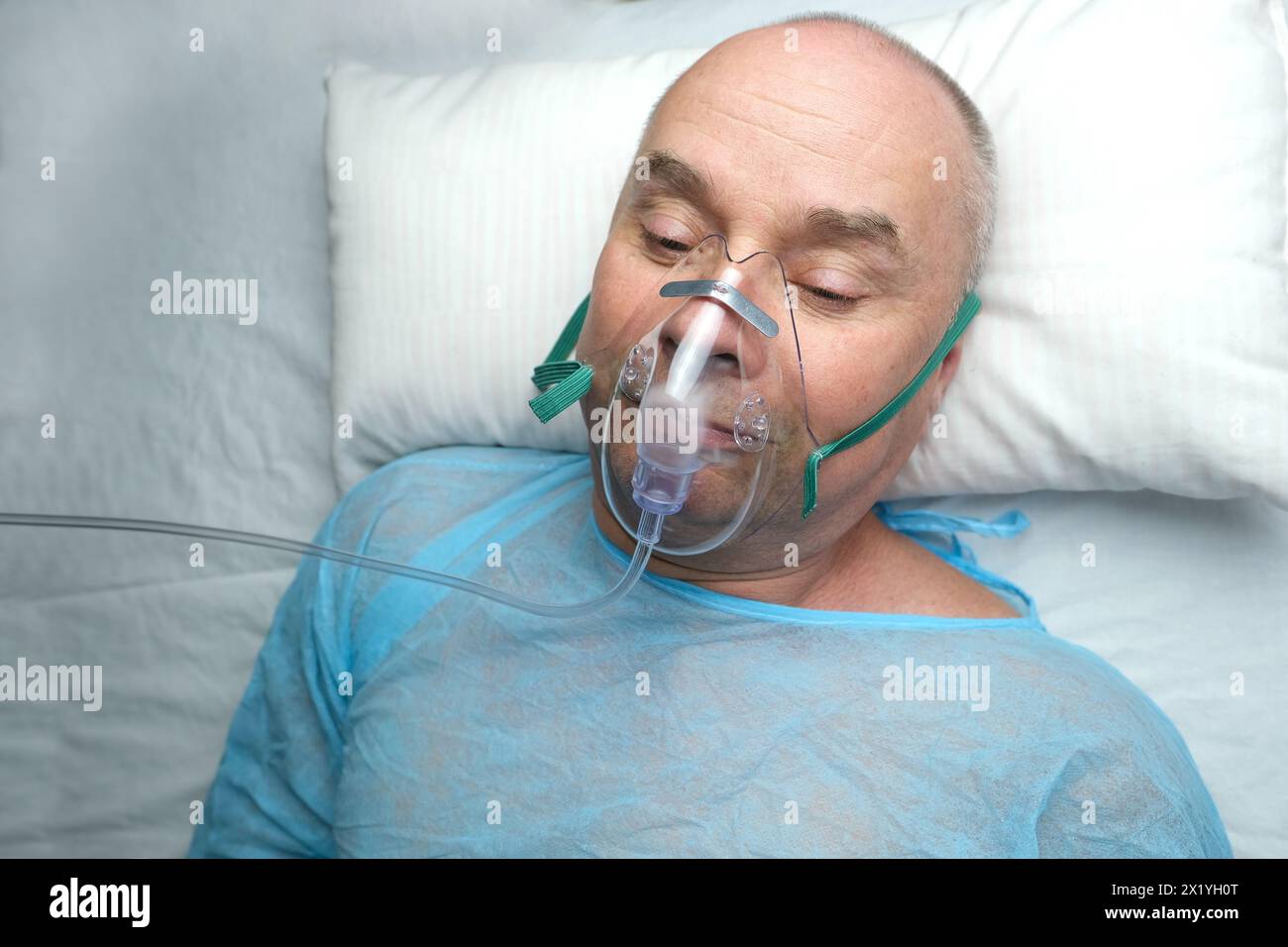 elderly man patient in a blue shirt lies in a facial oxygen mask, the ...