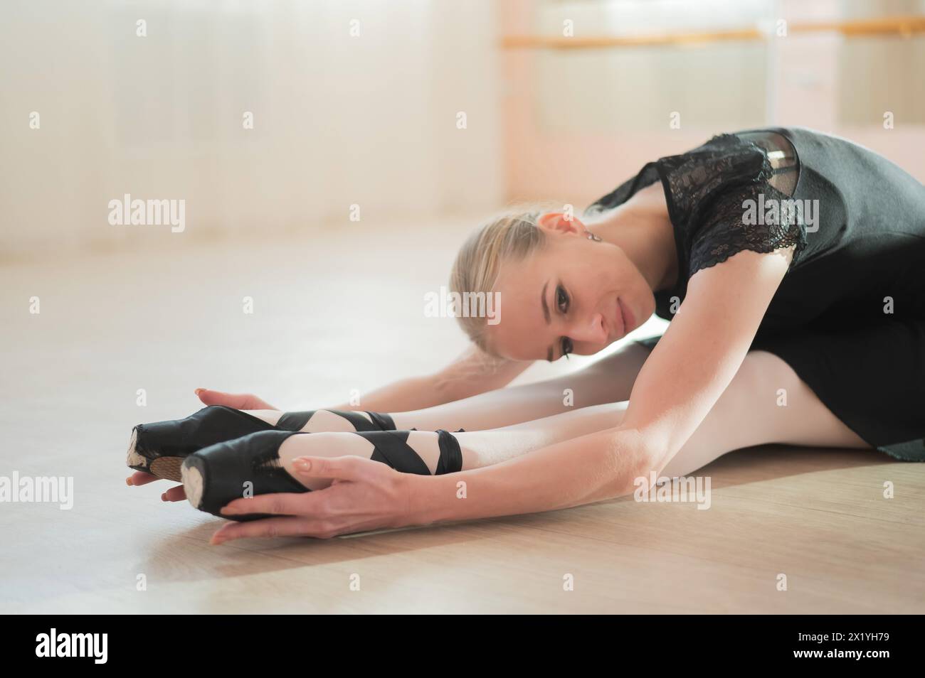 A young woman lies bent over on her feet in a ballet class. Ballerina ...