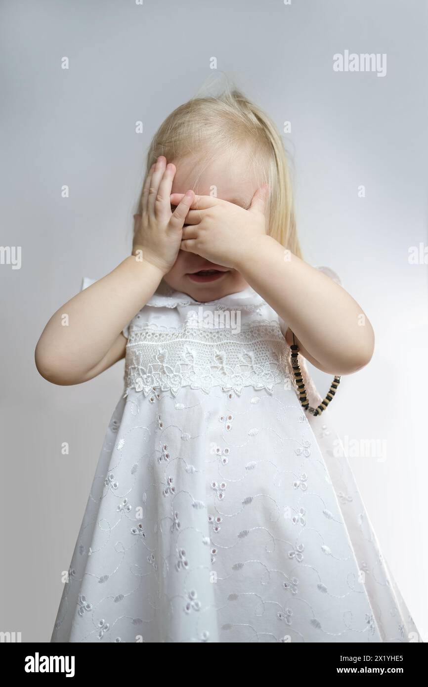 small child, a shy girl in a white dress covered her face with her ...