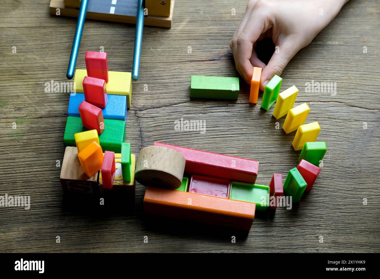 close-up of child's hand builds lines of dominoes, colored cubes of ...