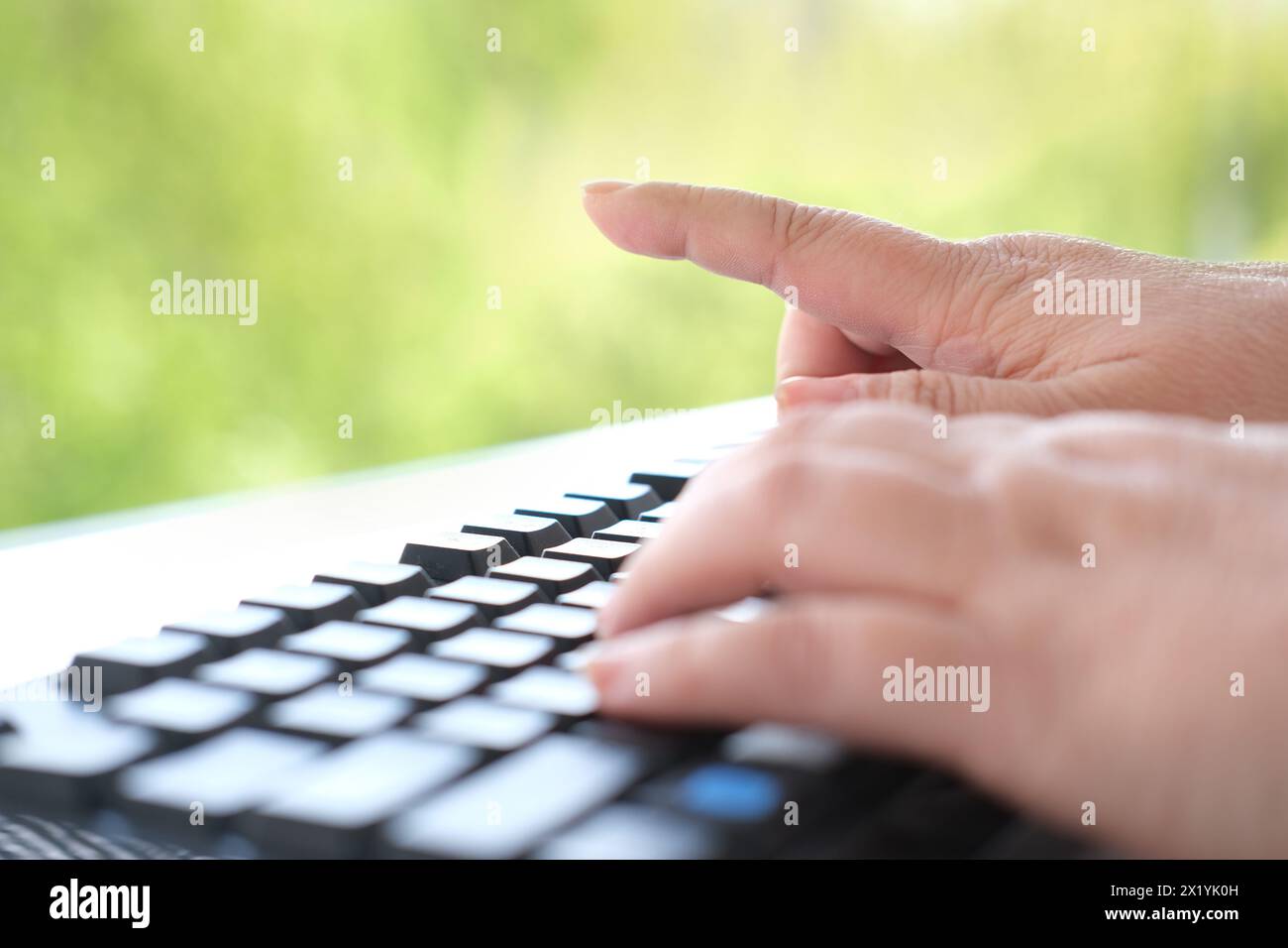 close-up female hand typing text on a computer keyboard on a natural background, workplace ...
