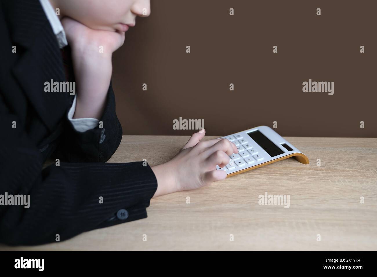 child, boy 8-9 years old in a black business suit makes calculations on ...
