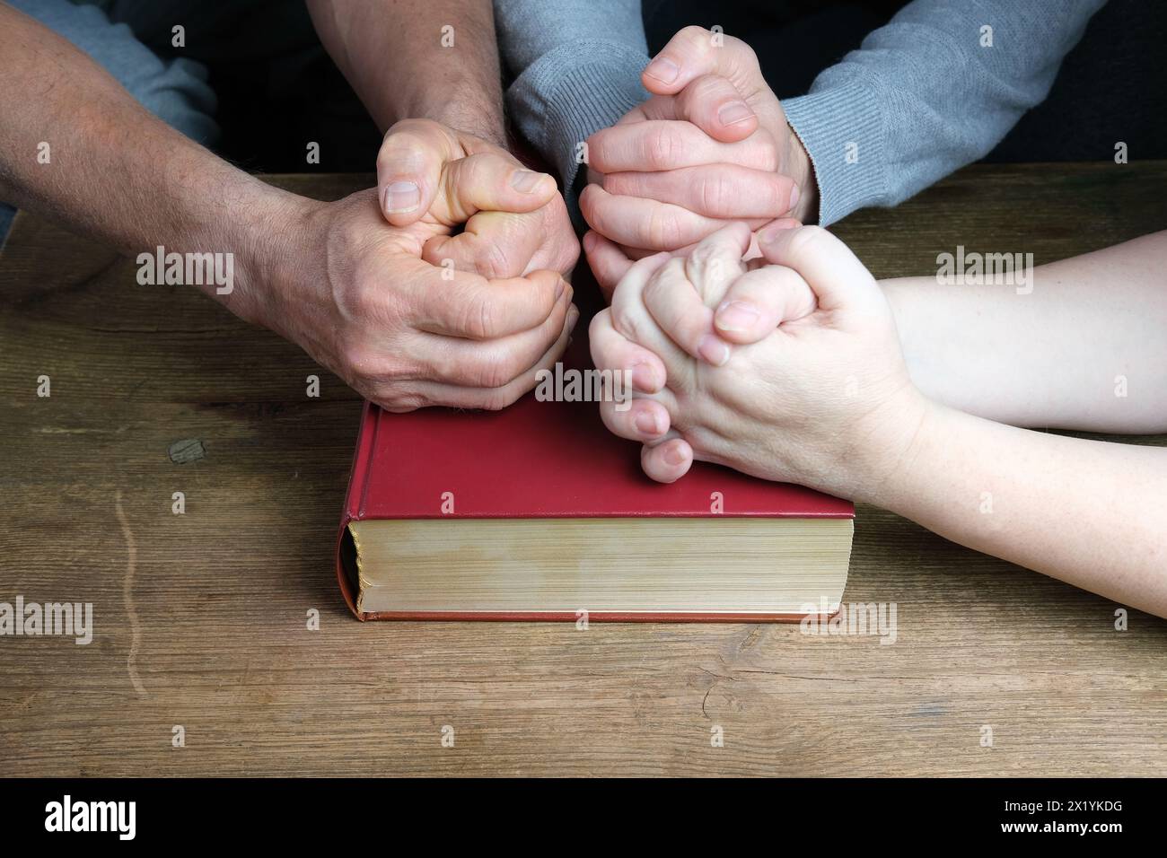 close-up of the hands of two men and a woman folded in a prayer gesture ...