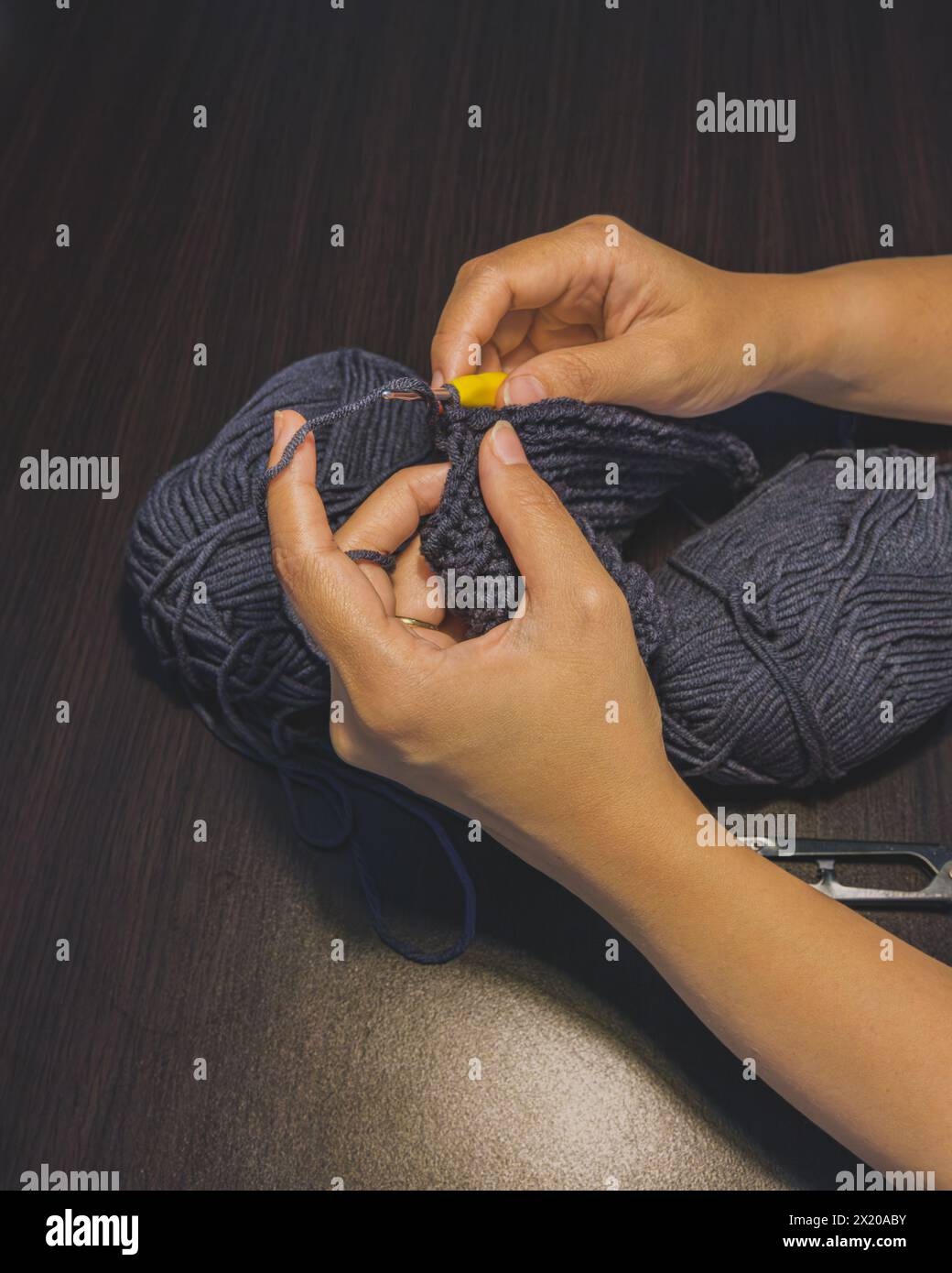 two hands holding a yellow crochete hook needle and knitting yarn ...