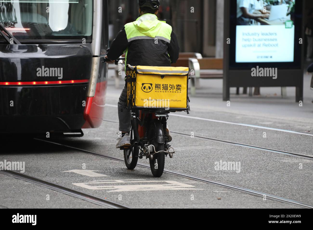 A Hungry Panda food delivery rider rides behind a light rail train on ...