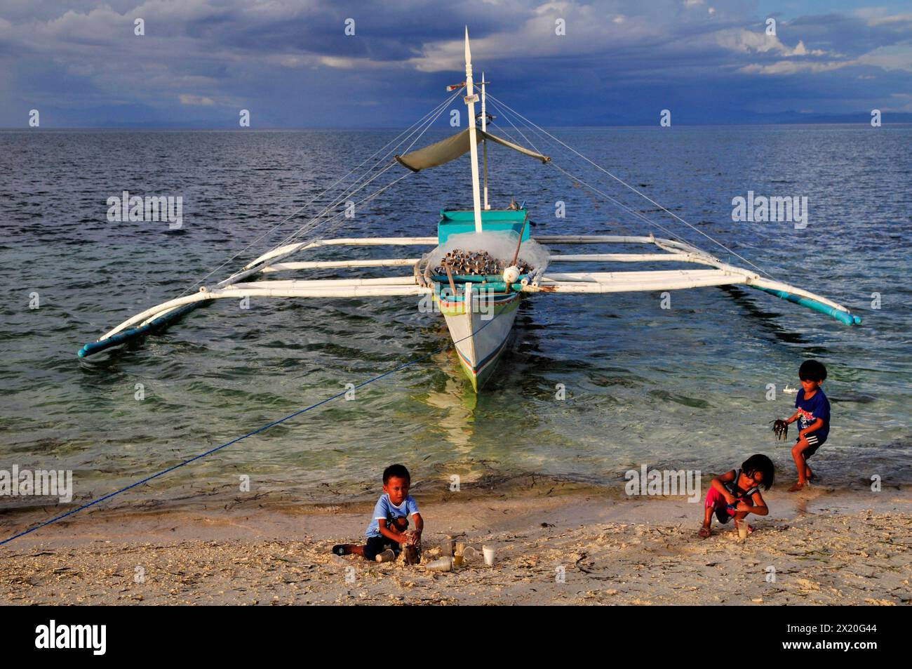 Children playing on the beach with a bangka boat behind them in ...
