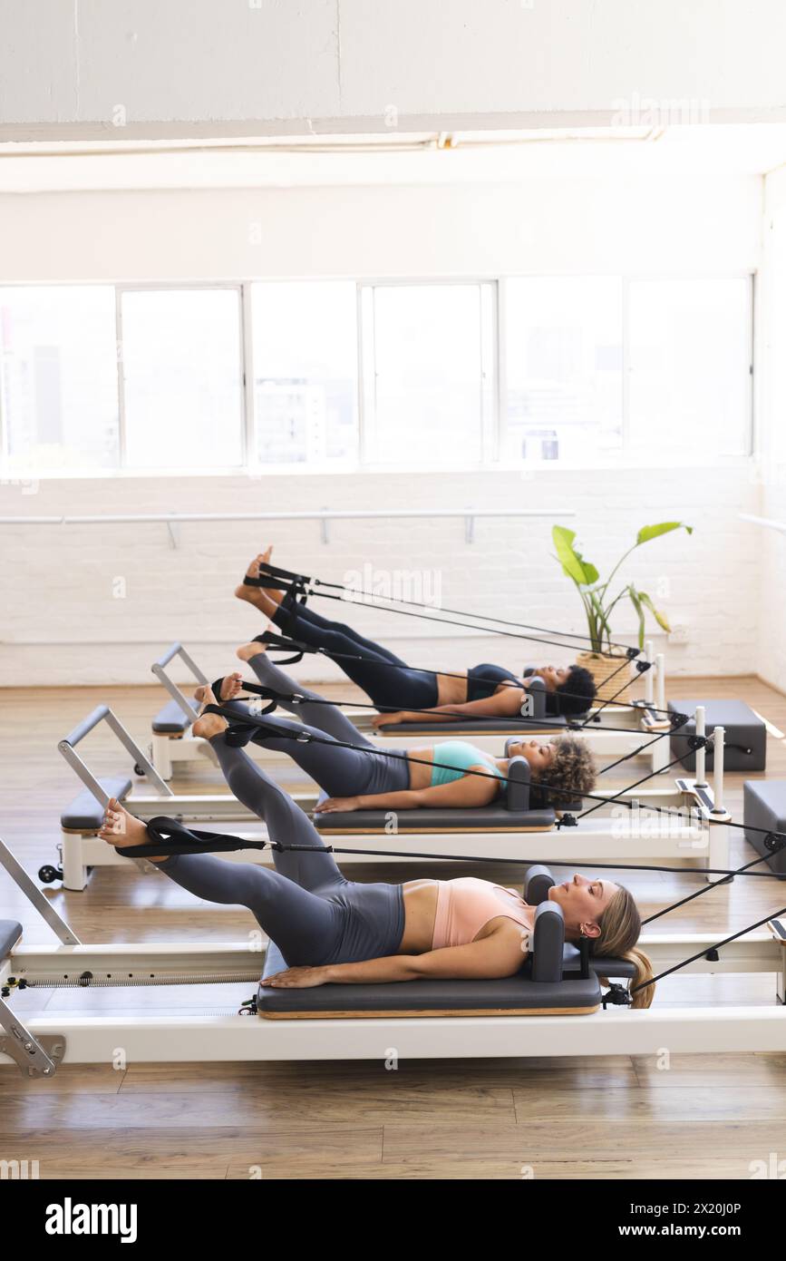 Three diverse women are using Pilates reformer machines in a bright ...