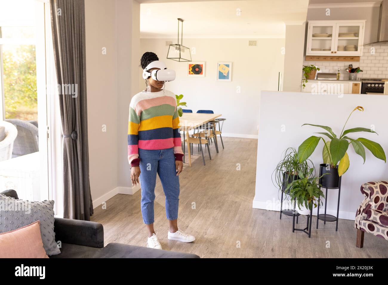 African American young woman in VR headset stands indoors in living ...