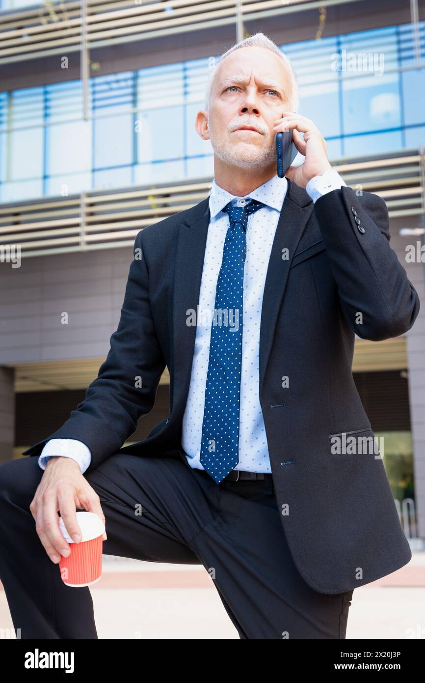 Businessman having a telephone conversation on his smartphone outdoors ...