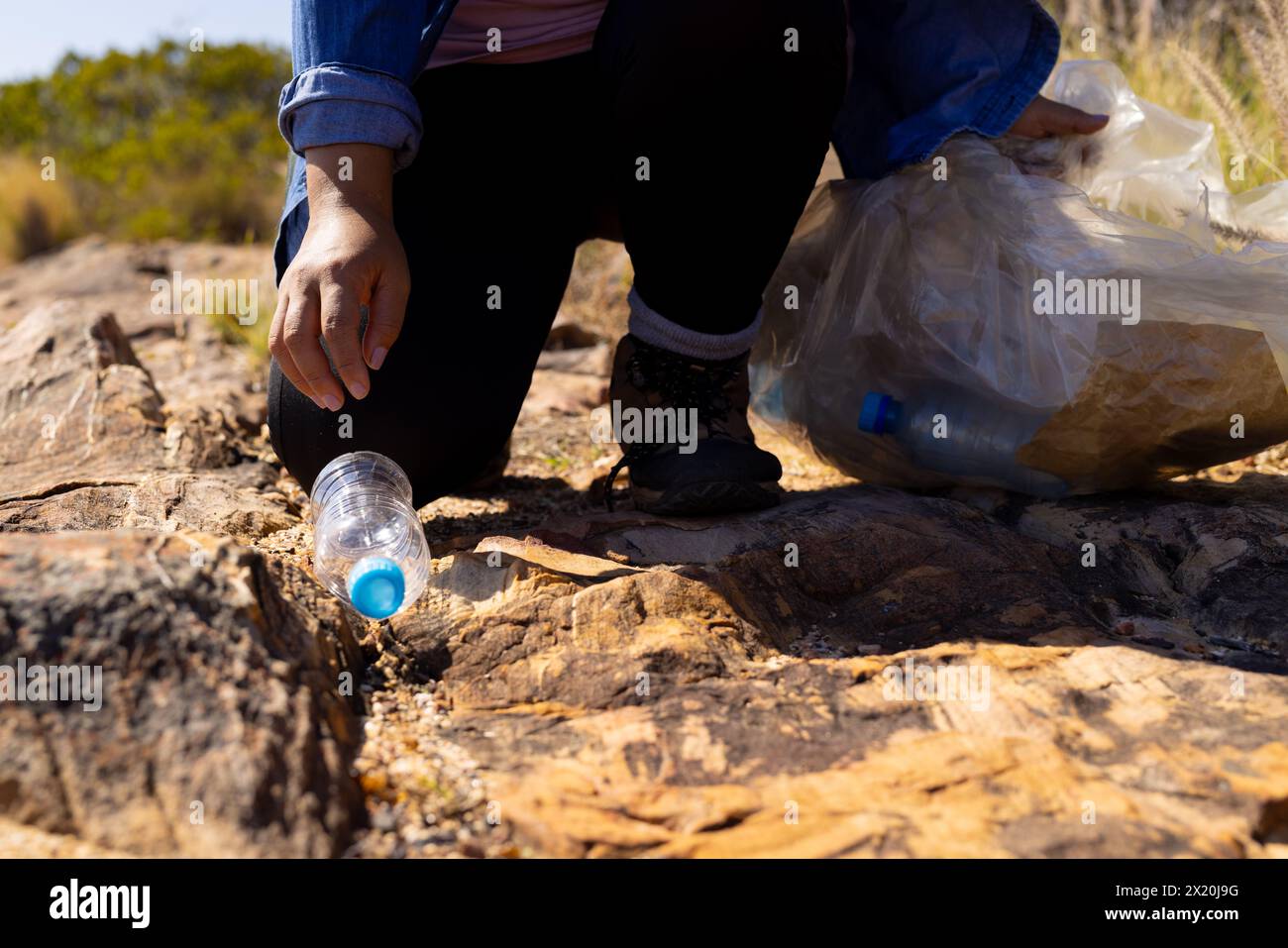 Biracial female hiker picking up trash, wearing casual outdoor gear ...