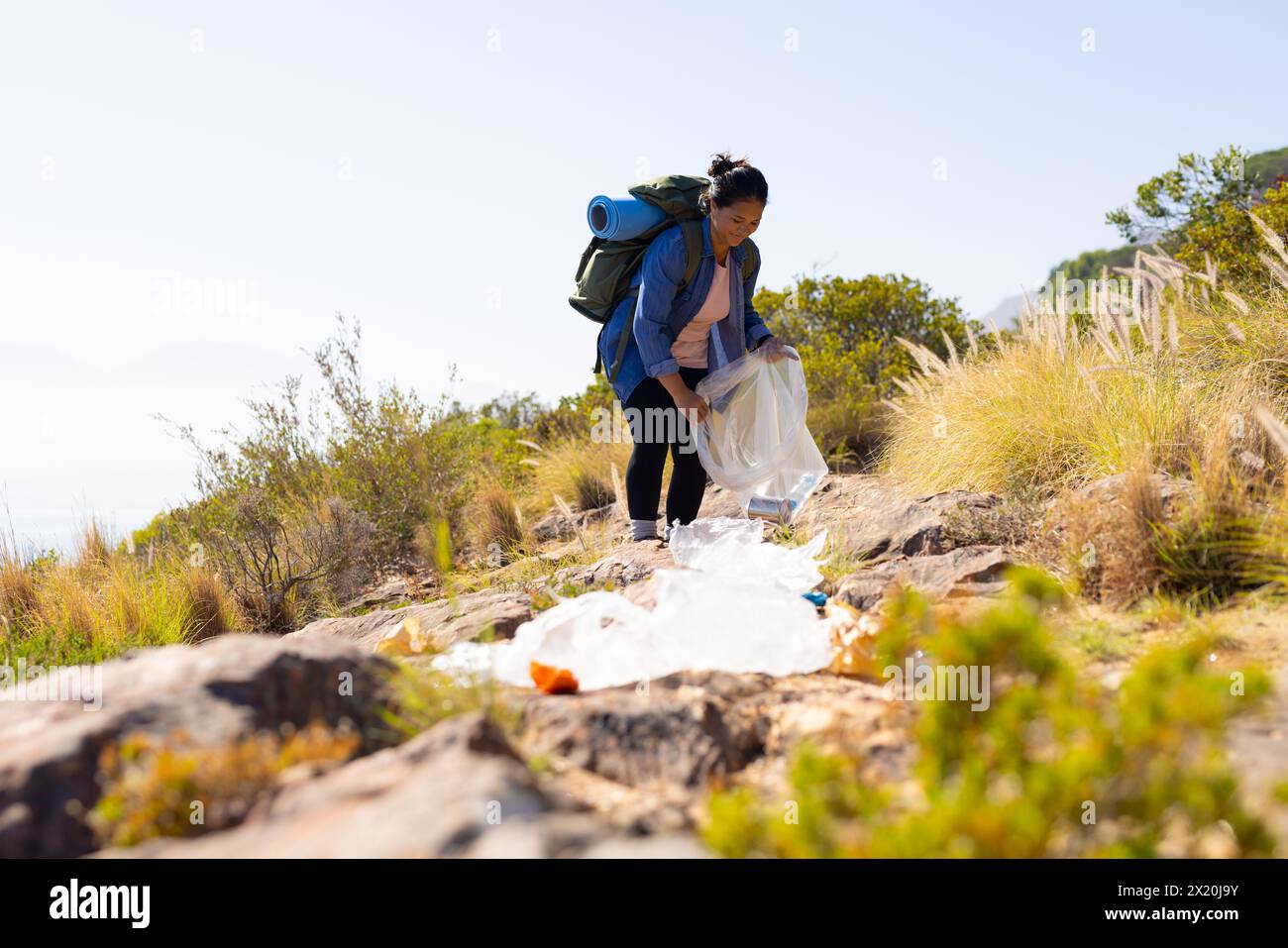 Biracial female hiker picking up trash on mountain trail adventure in ...
