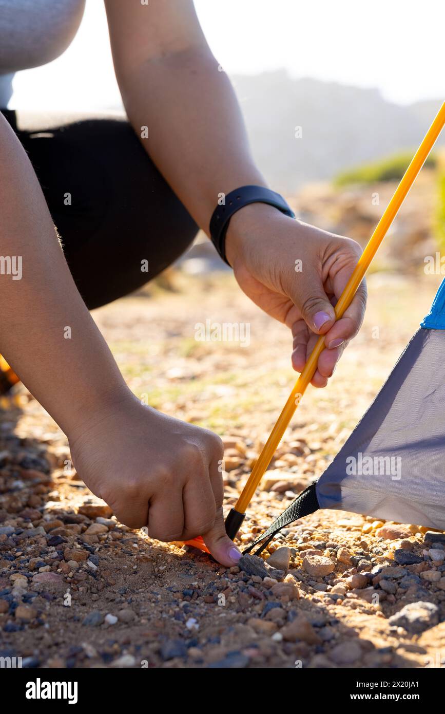 Biracial female hiker securing tent peg into the ground Stock Photo - Alamy