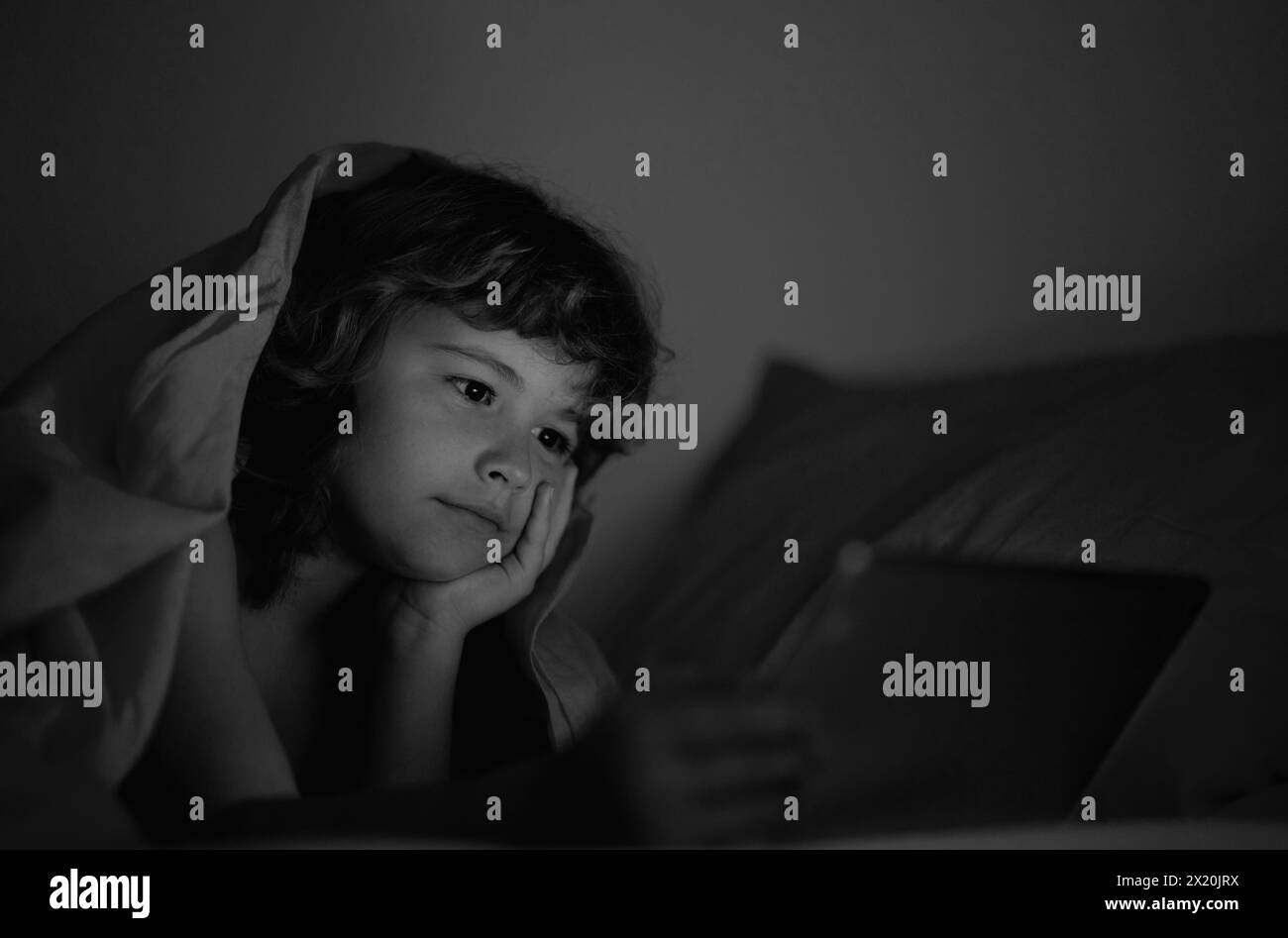 Kid alone at home. Kid lying in bed at night and playing digital tablet ...
