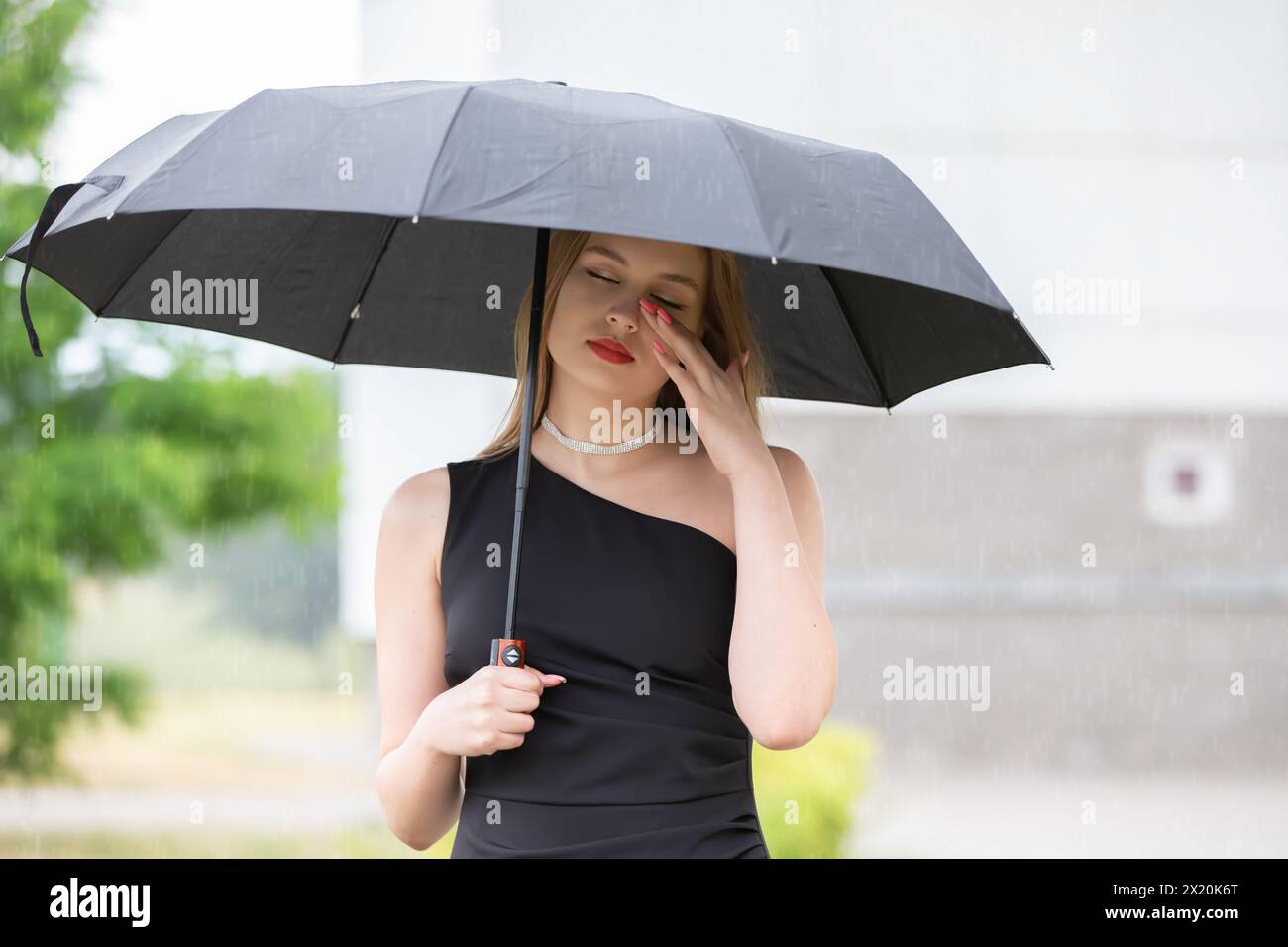 A girl wipes her tears under an umbrella in the rain. A girl in a black ...