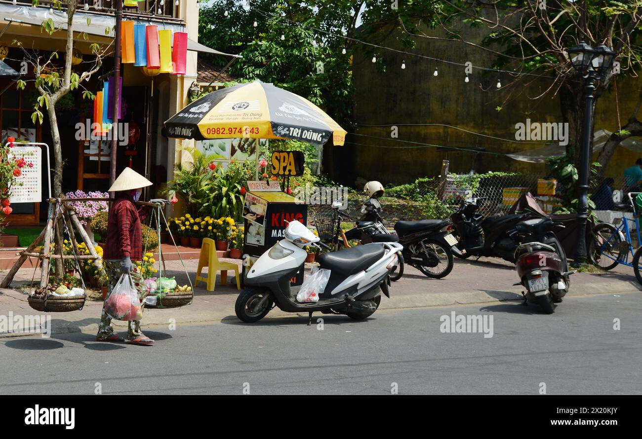 A woman carries a carrying pole with baskets with fruits, also called a ...