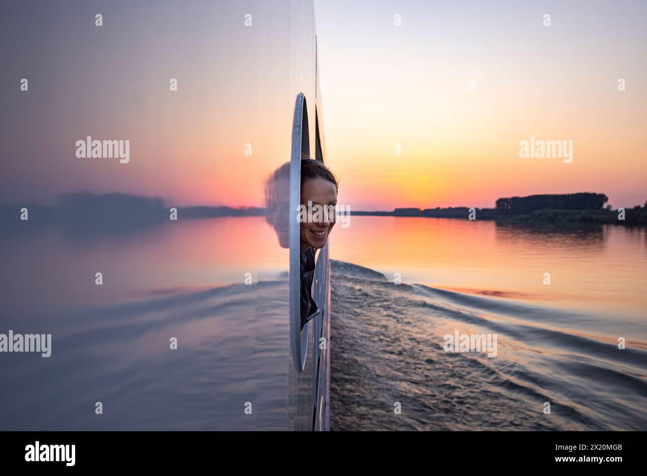 Smiling woman looking through window opening on board river cruise ship ...