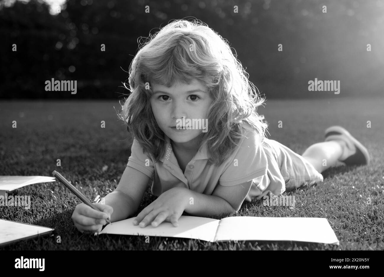 Cute lovely child with pencil writing on notebook outside. Kid read ...