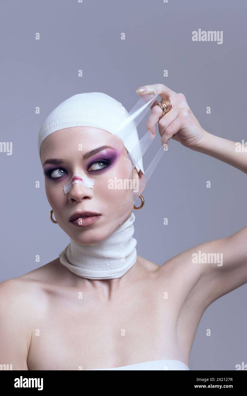 Woman with bright eye makeup unveiling bandage from face after plastic ...