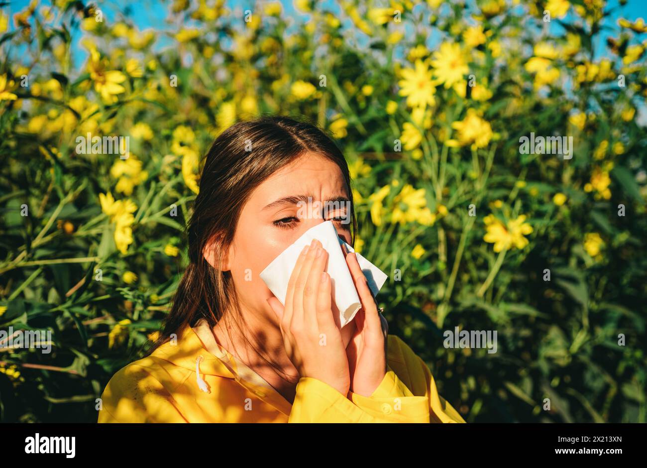 Sneezing young girl with nose wiper among blooming flowers in park ...