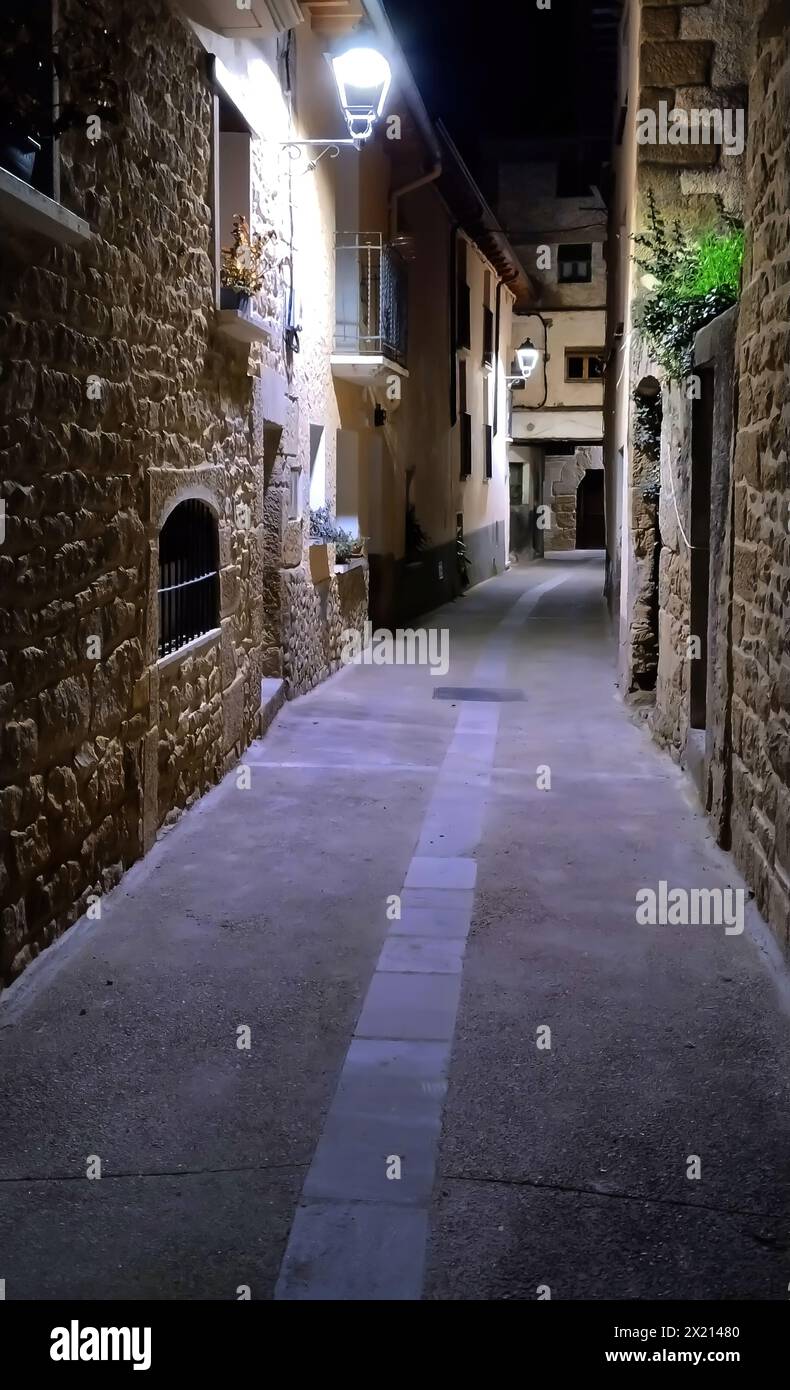 A narrow alleyway with brick houses on either side. The street is lit ...