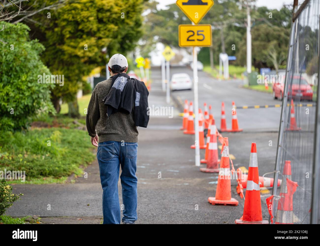Man walking on a pedestrian footpath. Orange traffic cones and metal ...