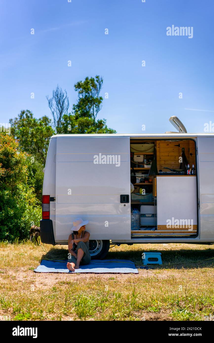 Woman sit in front of a camper van on a sunny day on a dry landscape ...