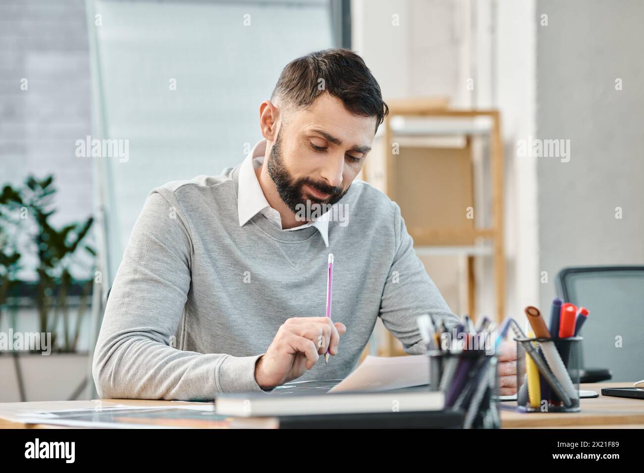 A man sitting at a desk, focused, with a pen in his hand, working on a ...