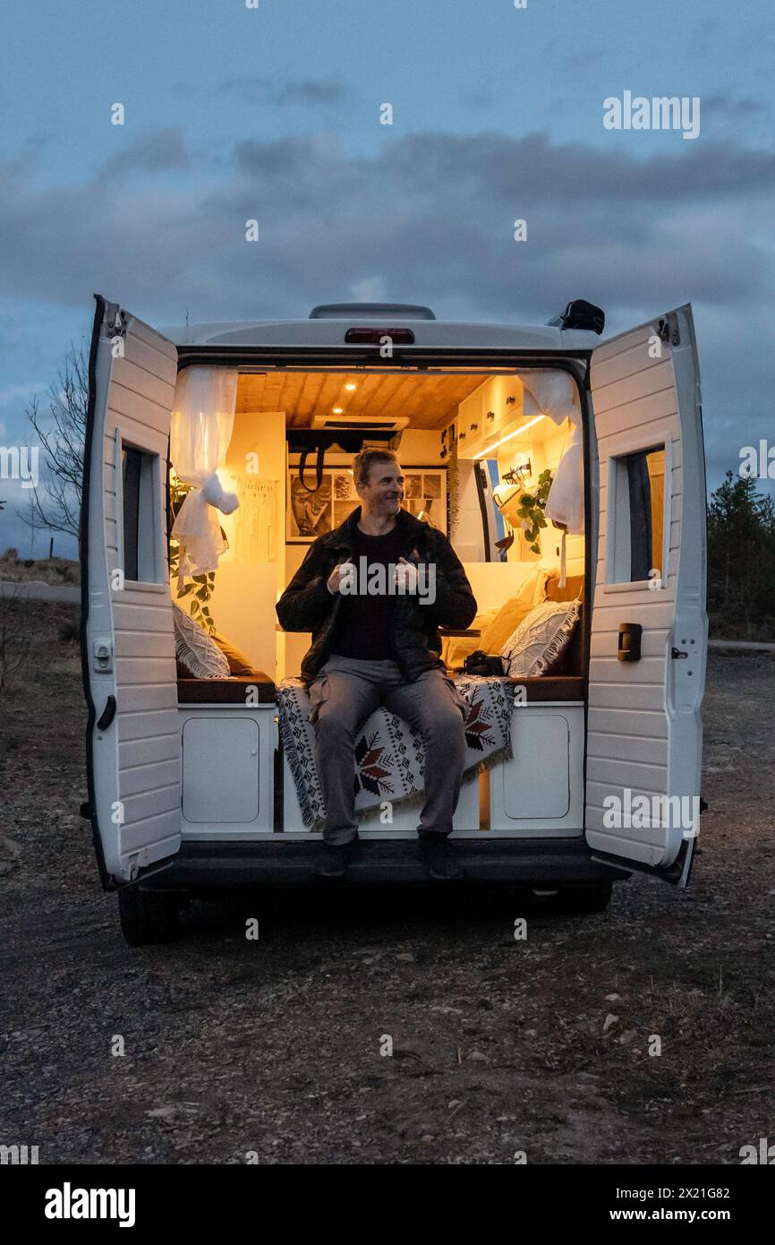 Mature man sitting in the back of a camper van during sunset. Concept ...
